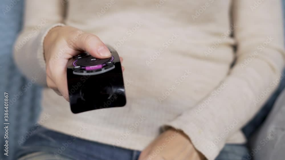 A Woman Switches Channels on the TV Using the Remote Control, Pressing ...
