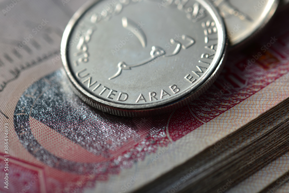 Extreme close up of one Dirham coin placed over hundred dirham note ...