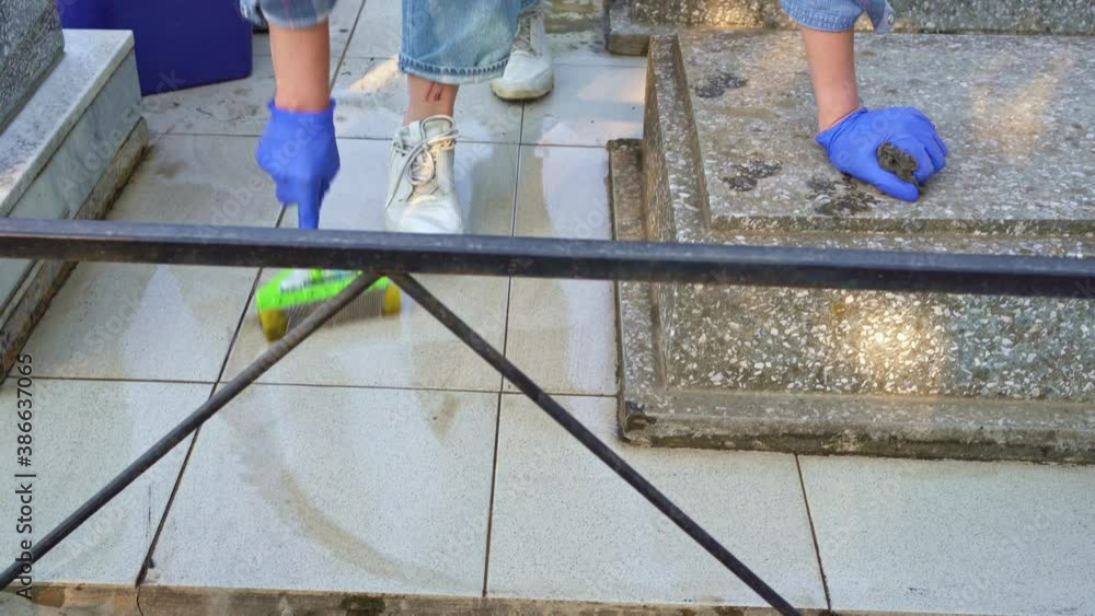 Cleaning cemetery. A woman washes grey paving slabs and monument grave ...