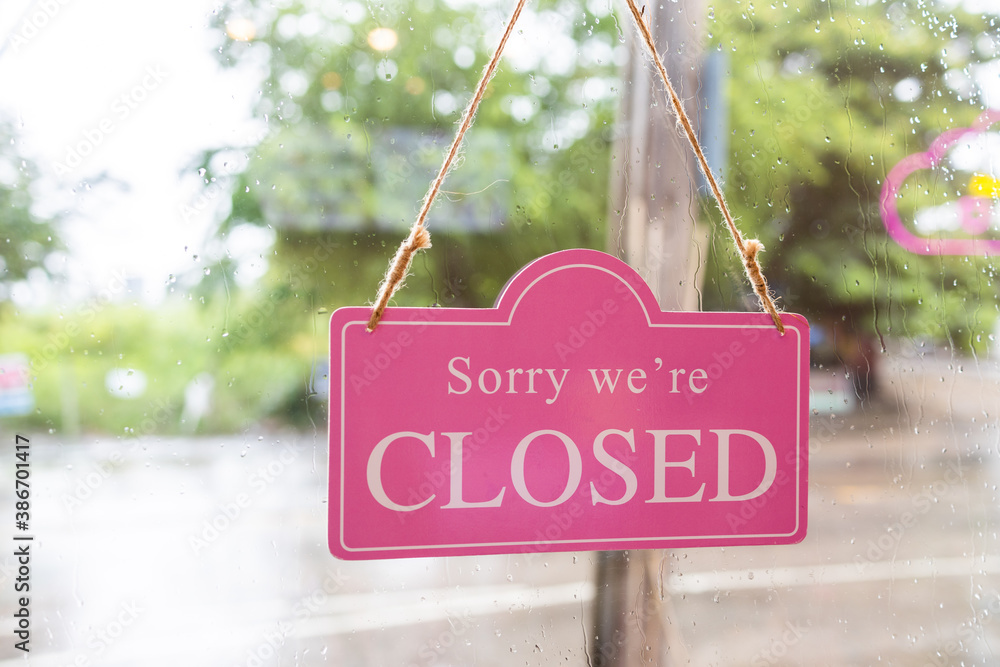 A pink sign with "Sorry we're closed" message hanging at glass door in ...