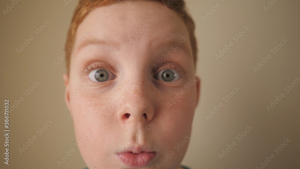 Little red-haired boy looking into camera with wow expression indoor ...