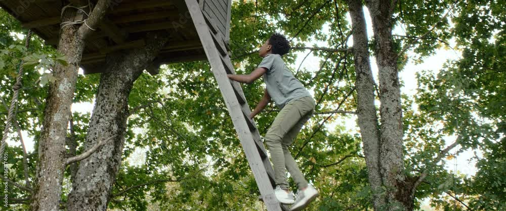 African-American kid climbing a ladder to meet his friends inside a ...