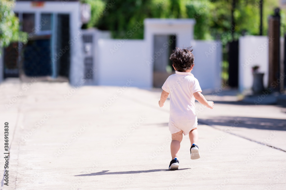 Back side of little boy was jogging on a concrete road. Summer morning ...