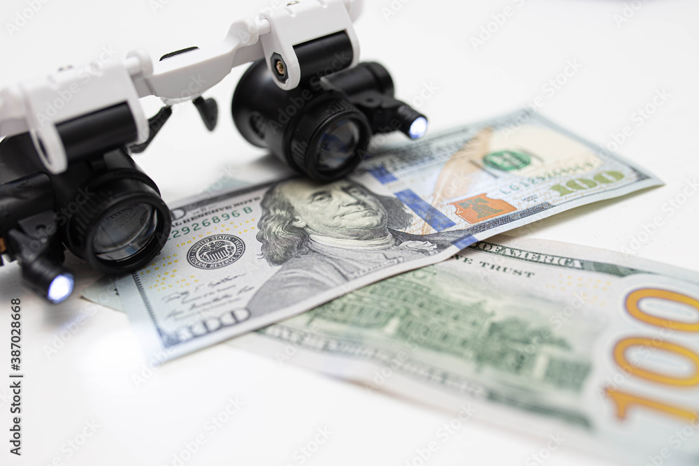 checking a hundred dollar bill with a magnifying glass, glasses with a ...