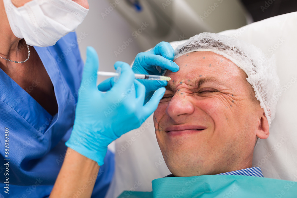 Female doctor is doing injection to patient in skin of face in estetic ...