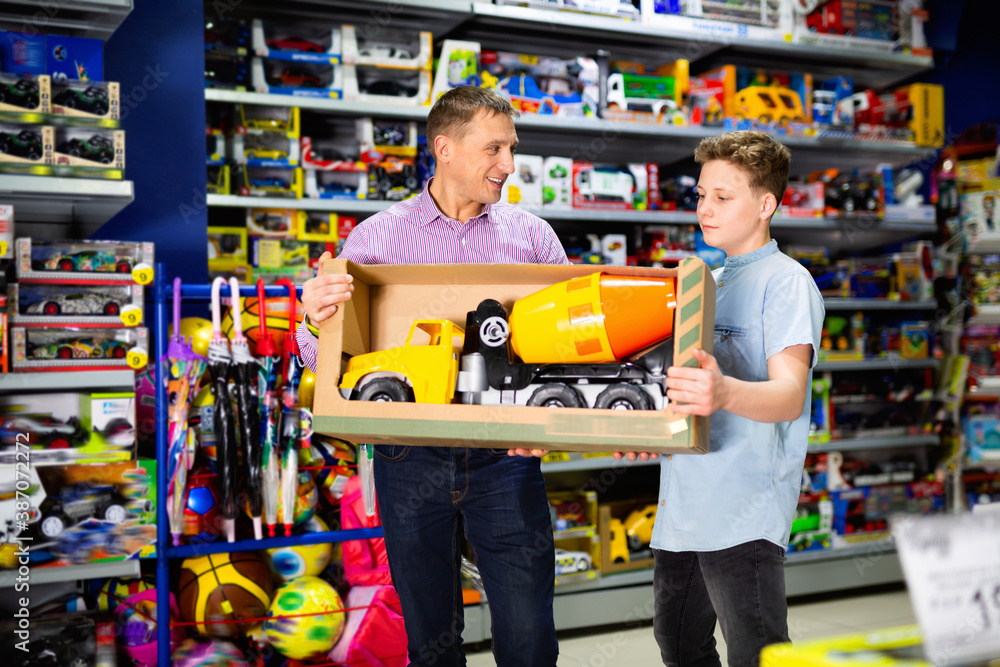 Happy positive smiling teen boy with father visiting children toy store ...