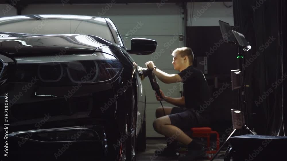 Side view of young man in working uniform doing car polish with ...