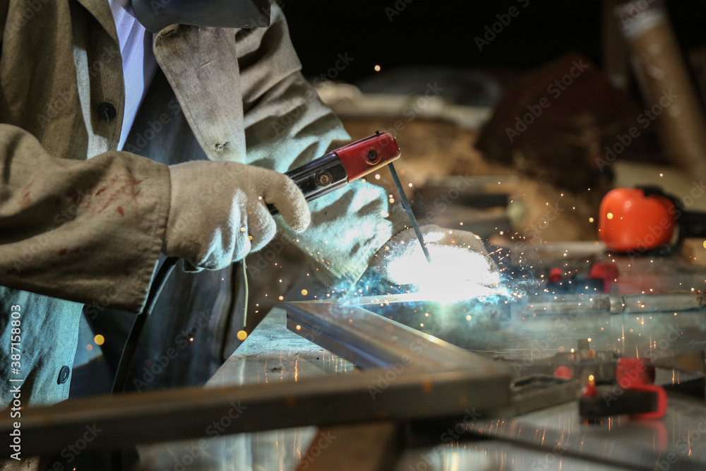 welder welds a metal structure in a workshop with electrical welding ...