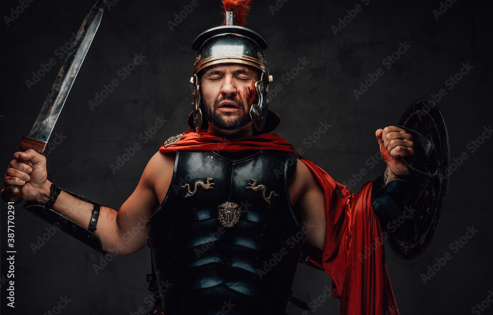 Brutal roman champion in dark armour with helmet and red cloak poses ...