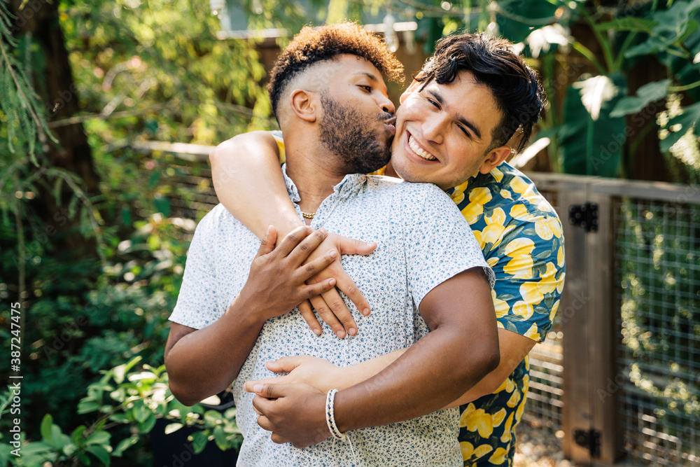Black man hugging and kissing latinx boyfriend in garden Stock Photo ...