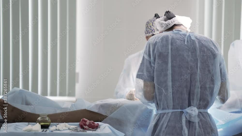 Rear view of a surgeon at work in operating room. Action. Side view of ...