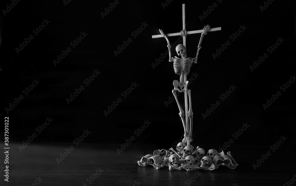 Skeleton tied up with crucifix wich has pile of skulls and bone below ...