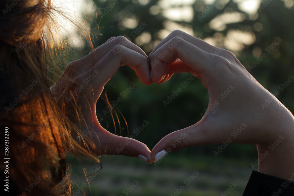 Young woman hands showing heart gesture against sunset light in field ...