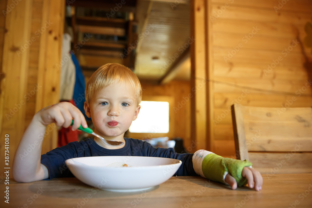Little boy with a broken wrist eating at the table. Boy with a plaster ...