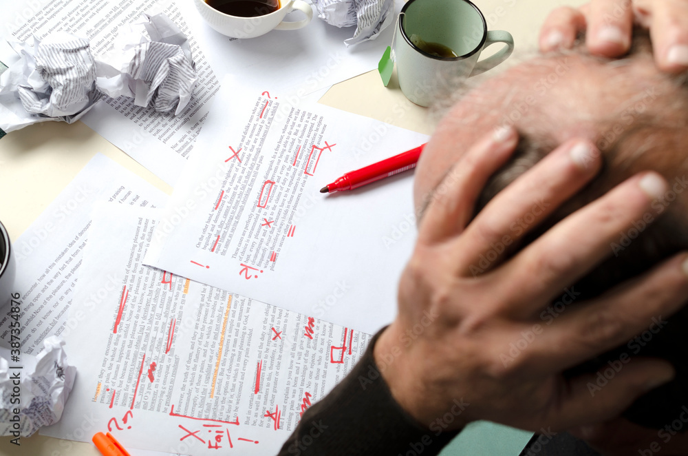Man holding his head and trying to deal with proofreading.Red marks on ...