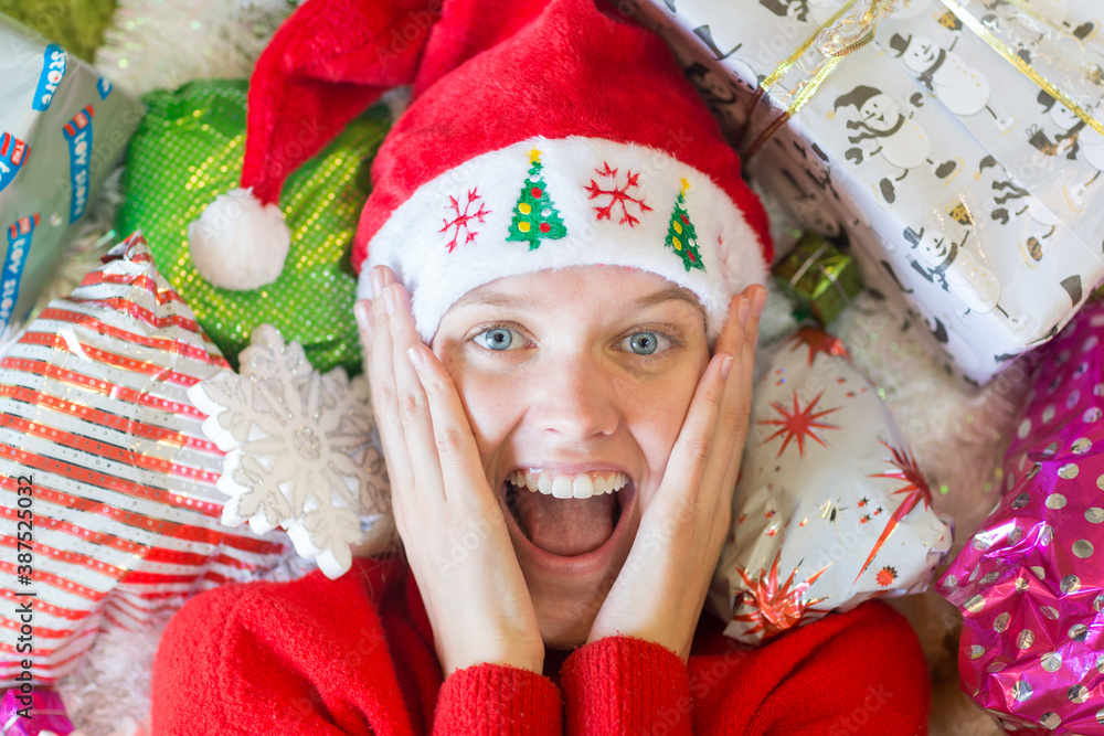 Christmas surprise! Excited amazed young woman lying next to many gifts ...