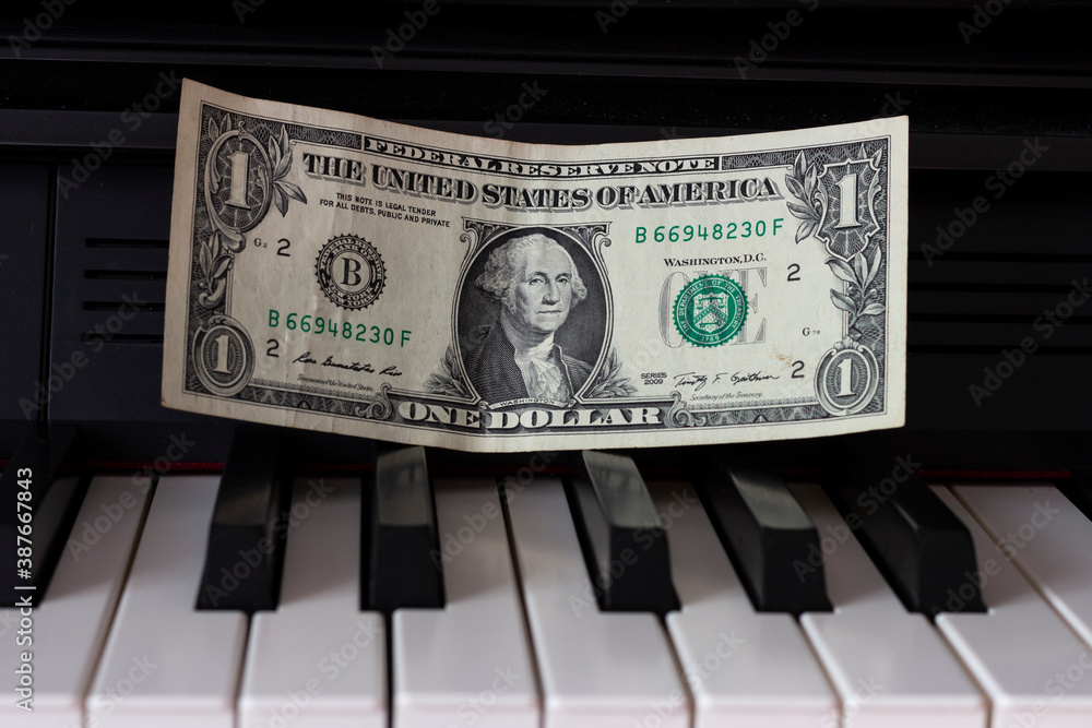 One dollar banknote lying on the piano keys. The dollar as a symbol of ...
