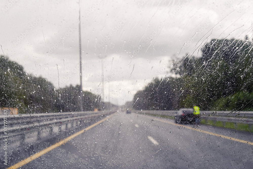 Road view through windshield car window with going rain drops during ...