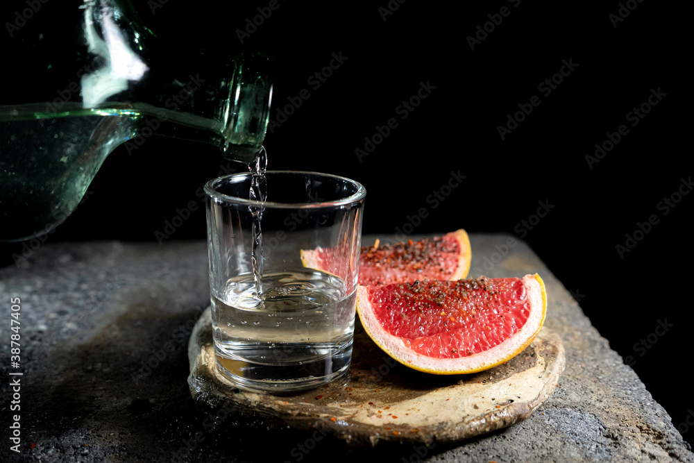 close up serving mezcal in a glass, on a rustic plate and grapefruit ...