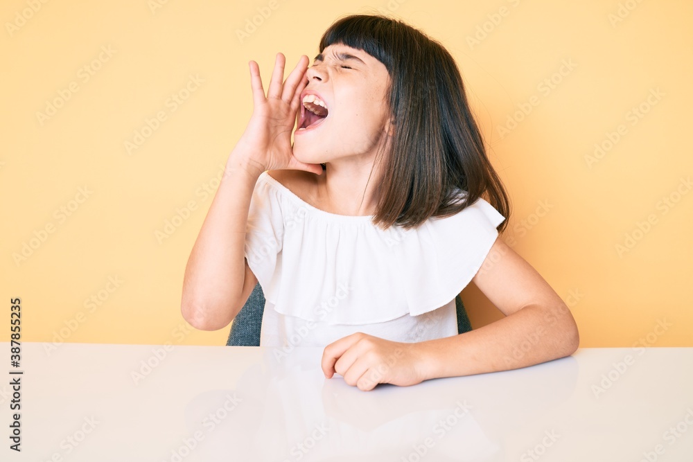 Young little girl with bang wearing casual clothes sitting on the table ...