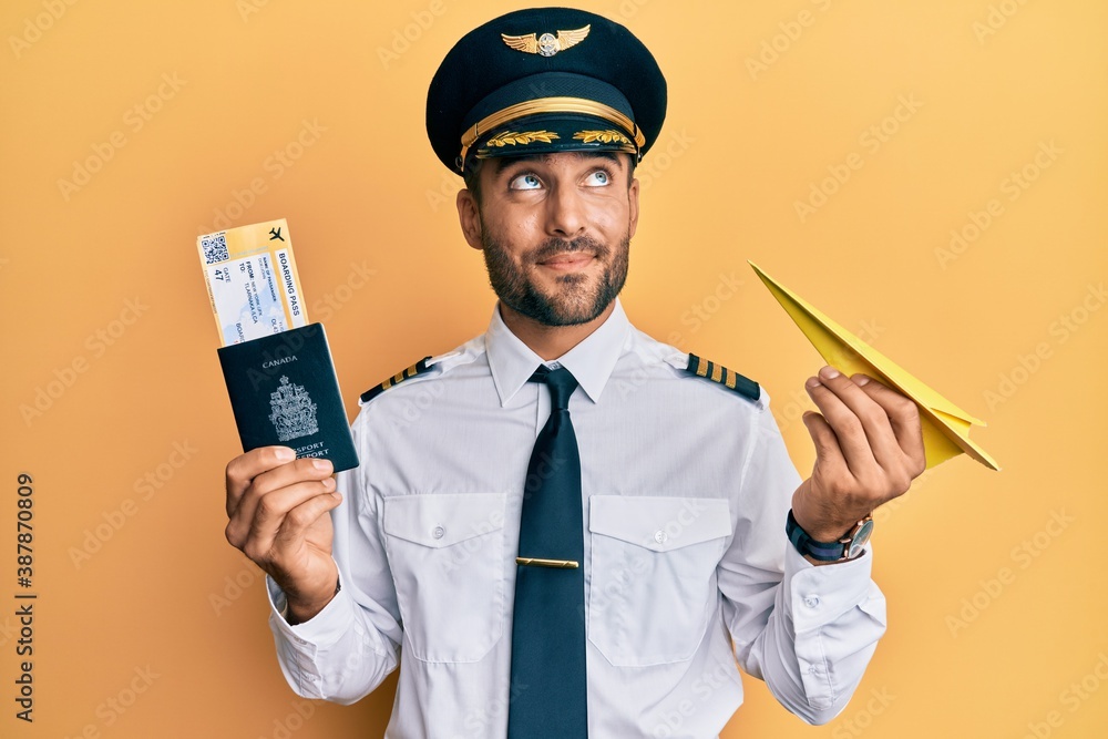 Handsome hispanic pilot man holding paper plane and passport smiling ...