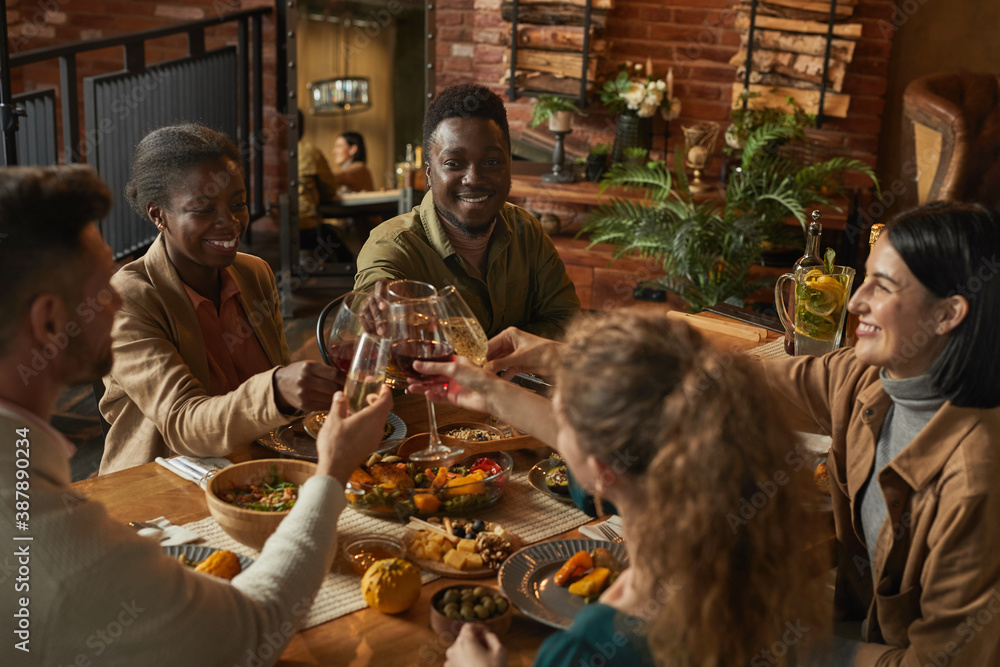 Diverse group of people clinking glasses while enjoying dinner party ...