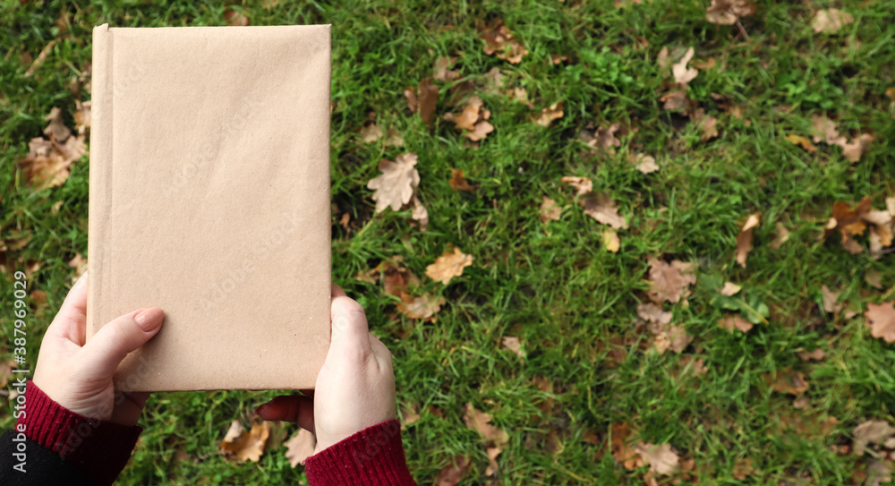 A closed book in a cover made of craft paper in female hands with green ...