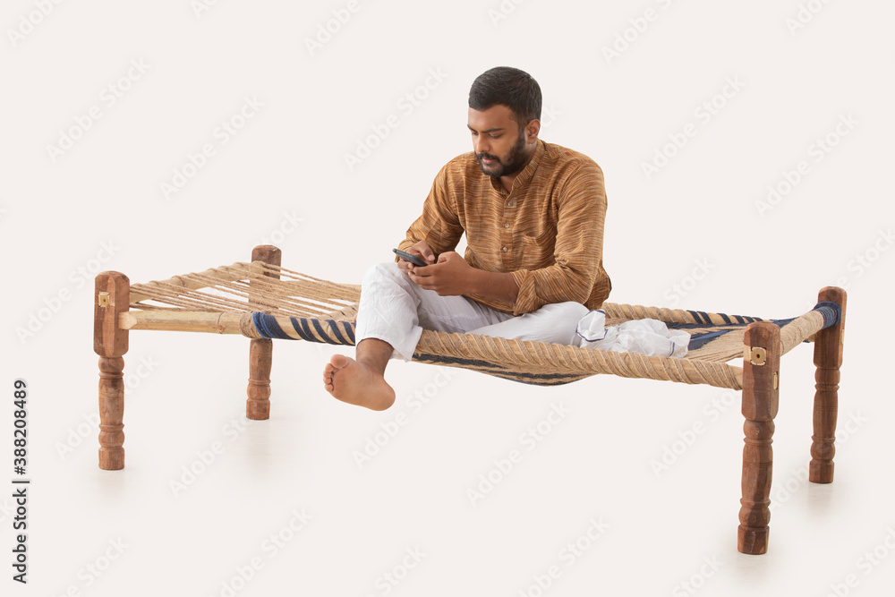 PORTRAIT OF A RURAL MAN SITTING ON A COIR COT AND USING MOBILE PHONE ...