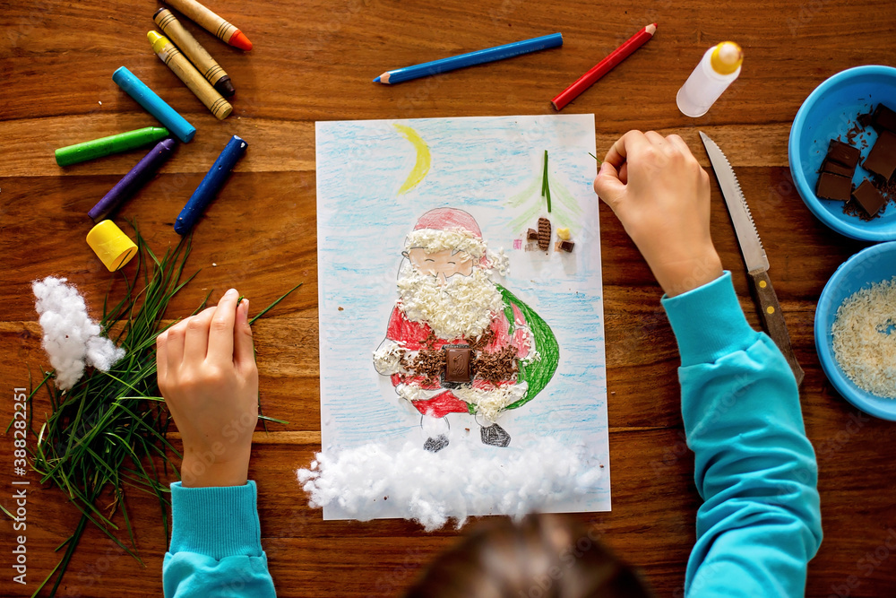 School child, boy, drawing a picture of Santa Claus and decorating him ...