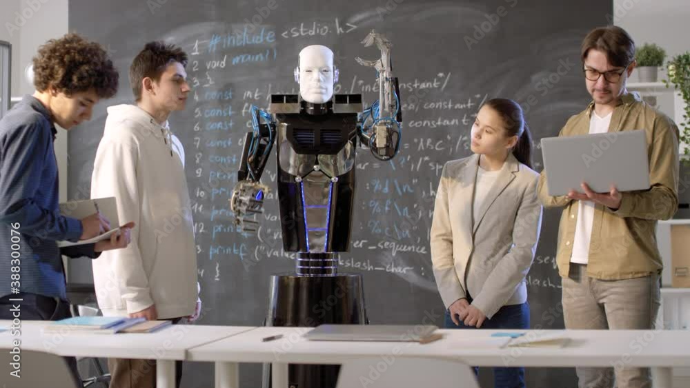 Activated humanoid robot standing between teenage students and IT ...