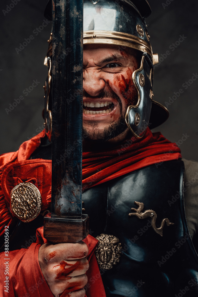 Savage roman barbarian with blood on his face looks at camera holding ...
