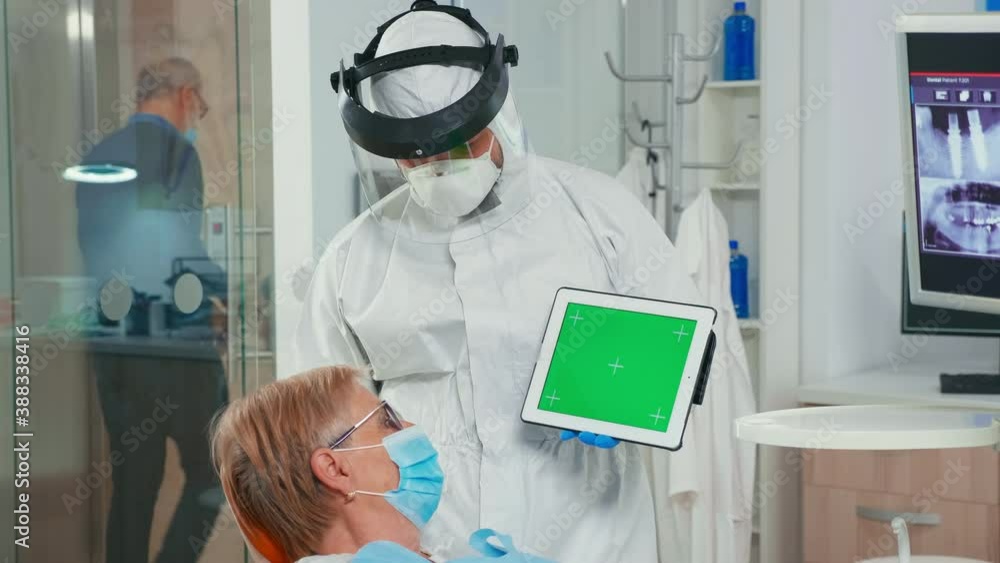 Dentist in coverall pointing at green screen display during coronavirus ...