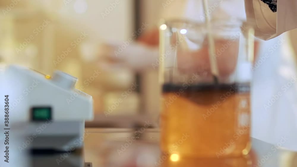 gloved hands in the lab stirring the liquid in the beaker, the other ...