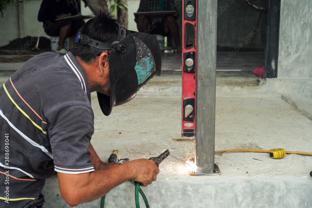 Welder with face shield is welding the steel column with the plate on ...