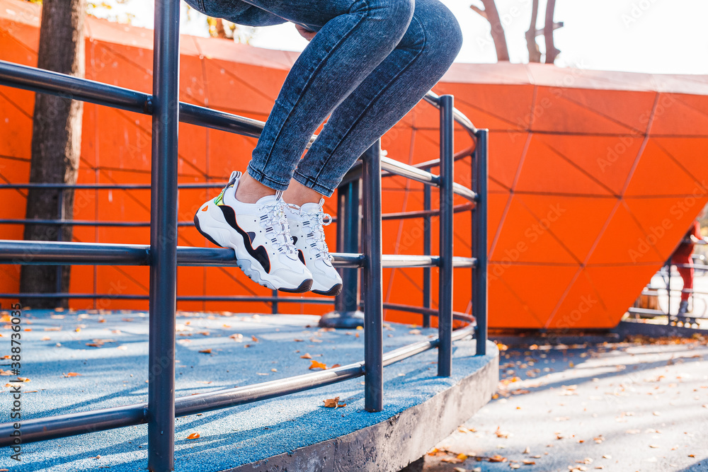 Legs of a girl in jeans and white sneakers with black inserts who sits ...