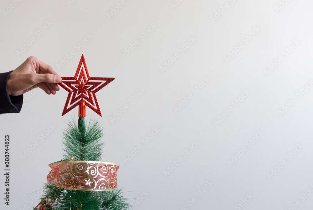 hand placing a red christmas star on top of a small christmas tree to ...