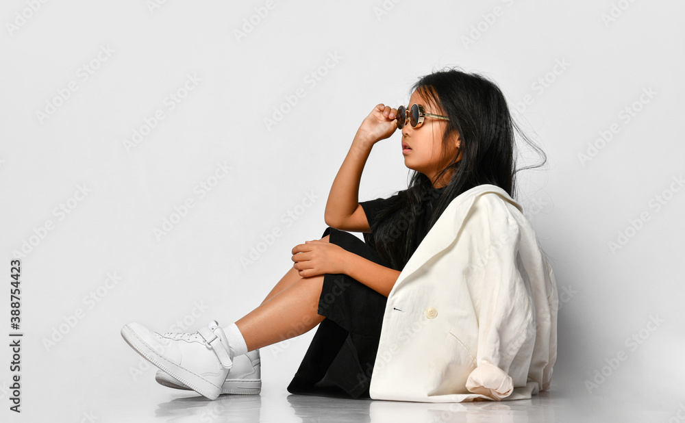 Side view of a little stylish girl model posing in the studio taking ...