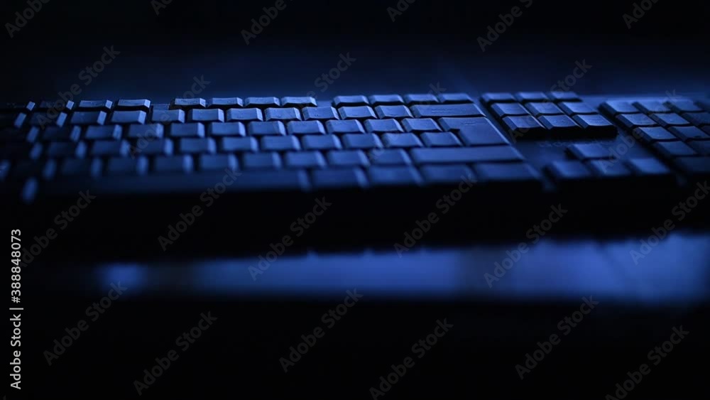 A computer keyboard in the dark night in blue LIGHT. Focus follows the ...