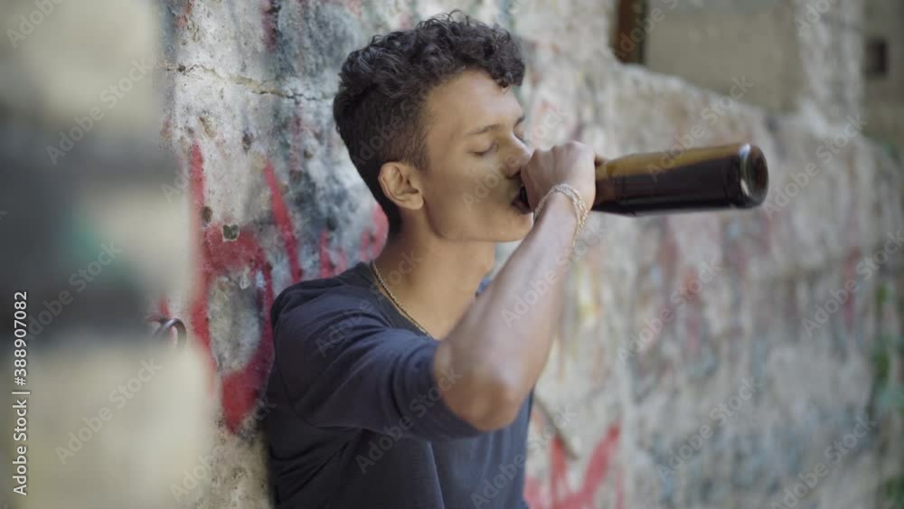Side view of teenage mixed-race boy drinking beer on ruins outdoors ...
