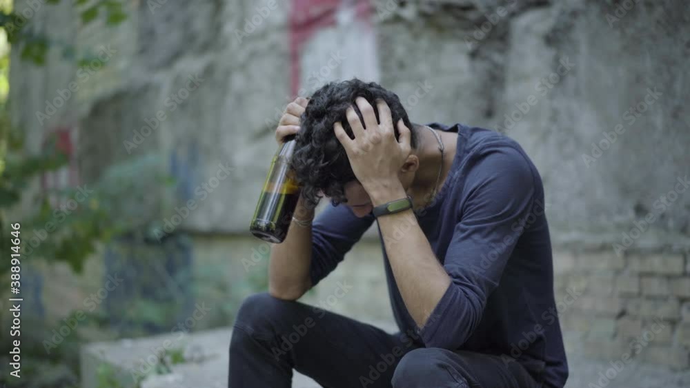 Vidéo Stock Frustrated teenage boy drinking beer at slum and crying ...