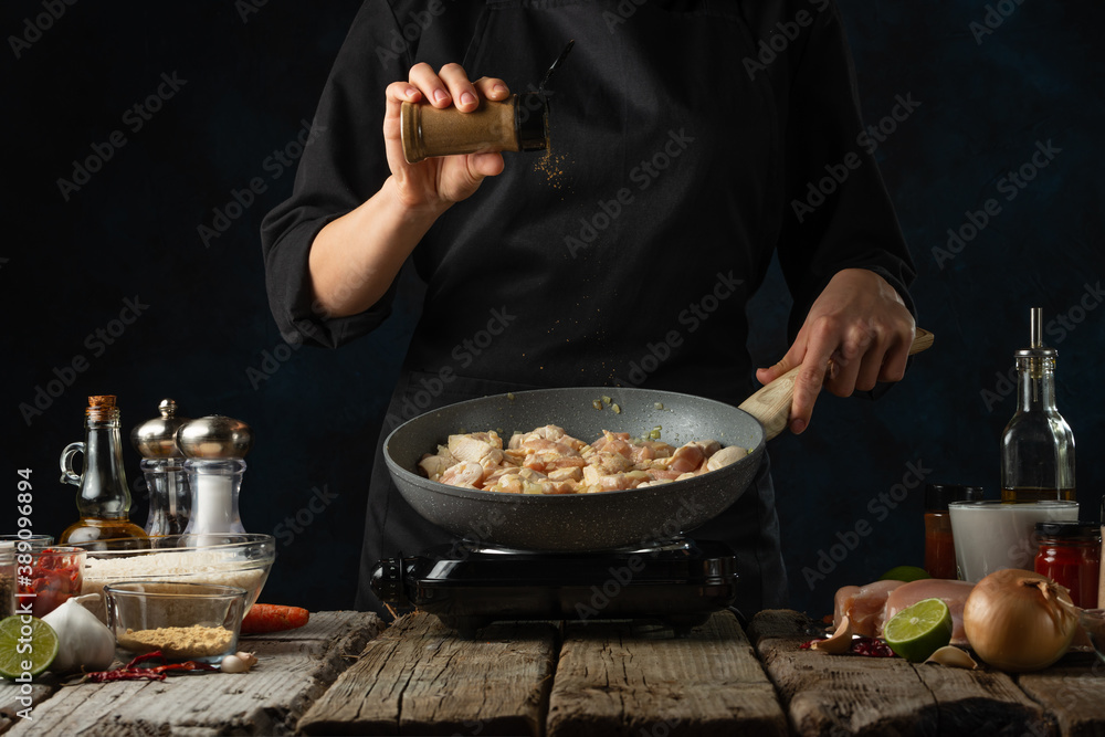 Professional chef pours spices to pan wok with frying chicken ...