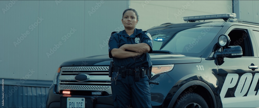 Mixed race female police officer posing against police car with ...