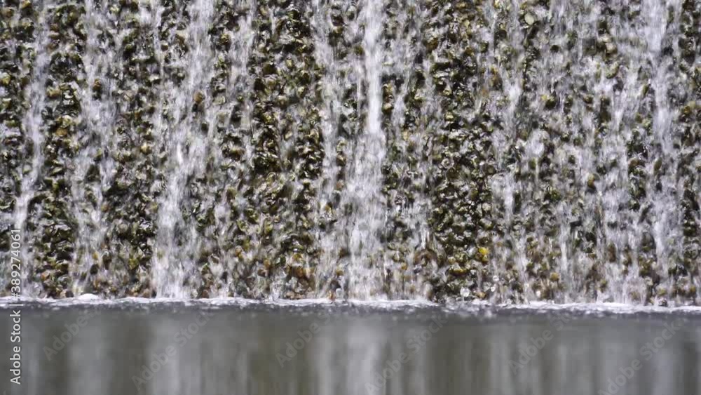 Water falling pouring into a poolside from stone wall, close up ...