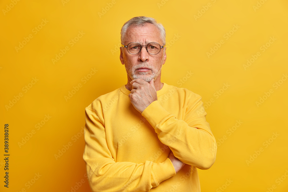 Serious looking puzzled bearded grey haired handsome man holds chin and ... Serious looking puzzled bearded grey haired handsome man holds chin and ...