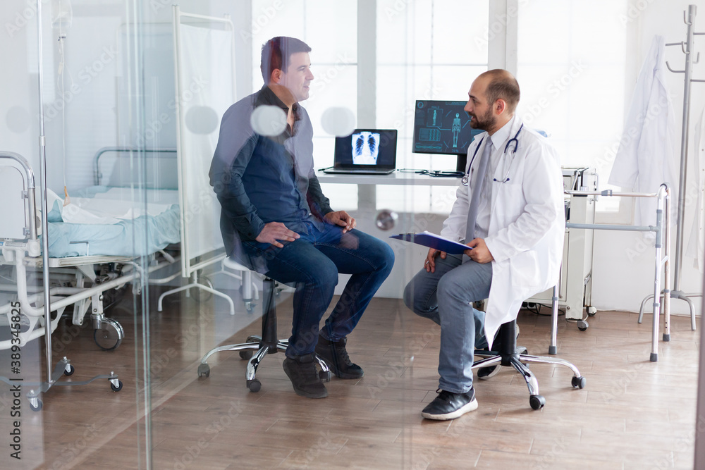 Doctor consulting young man in hospital examination room wearing white ...