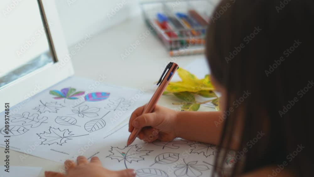 Little girl coloring different types of leaves on a paper sheet with a ...