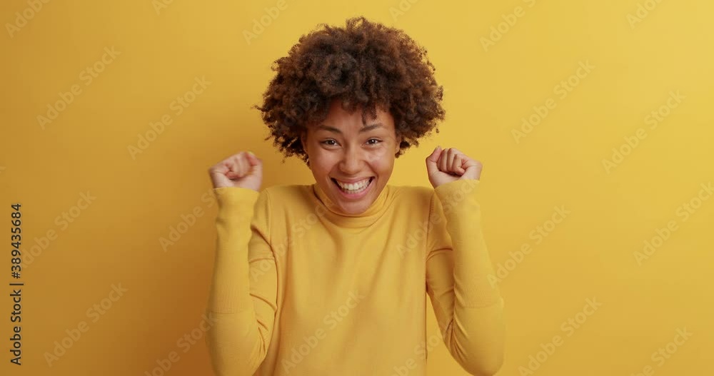 Overjoyed dark skinned woman with curly hair makes fist bump shows ...