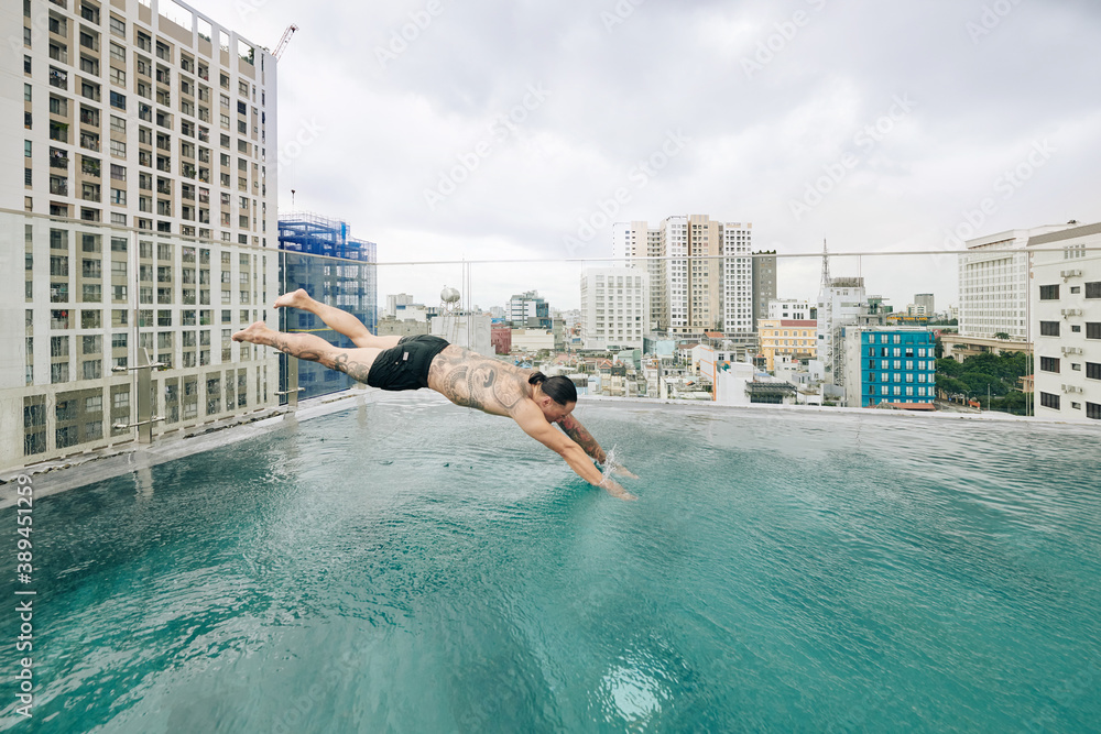 Fit young man jumping in infinity swimming pool on rooftop of ...
