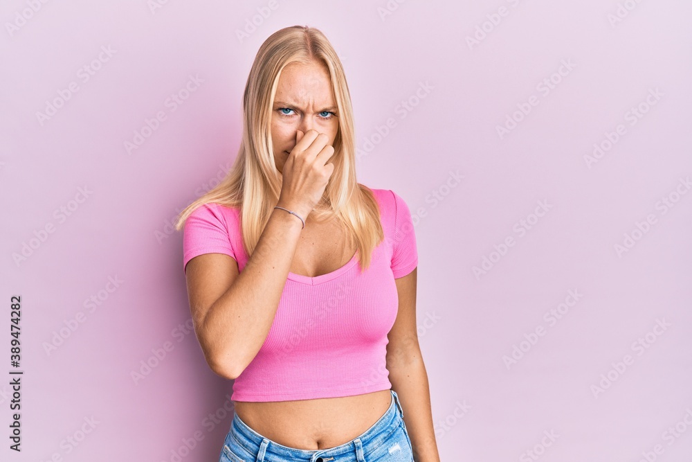Young blonde girl wearing casual clothes smelling something stinky and ...