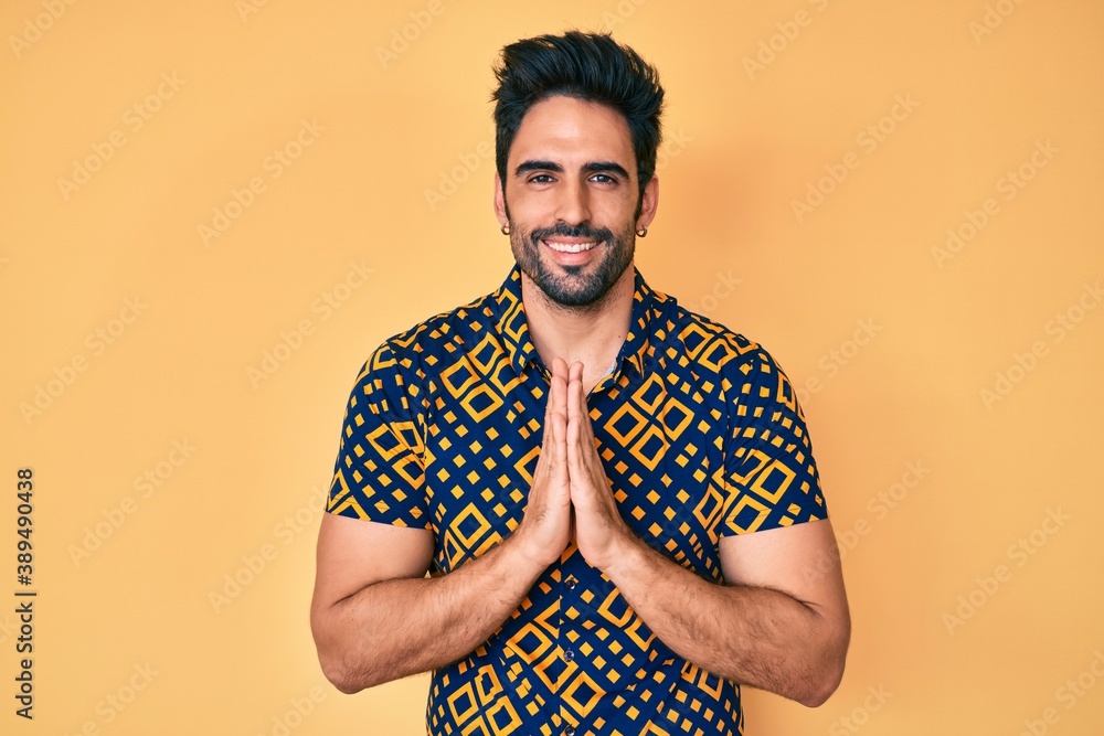 Handsome hispanic man with beard wearing 80s disco style shirt praying ...